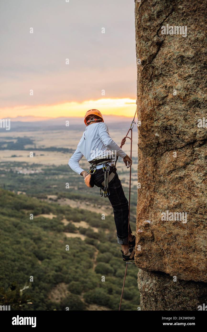 Male mountaineer climbing high cliff with safety carabiner and ropes ...
