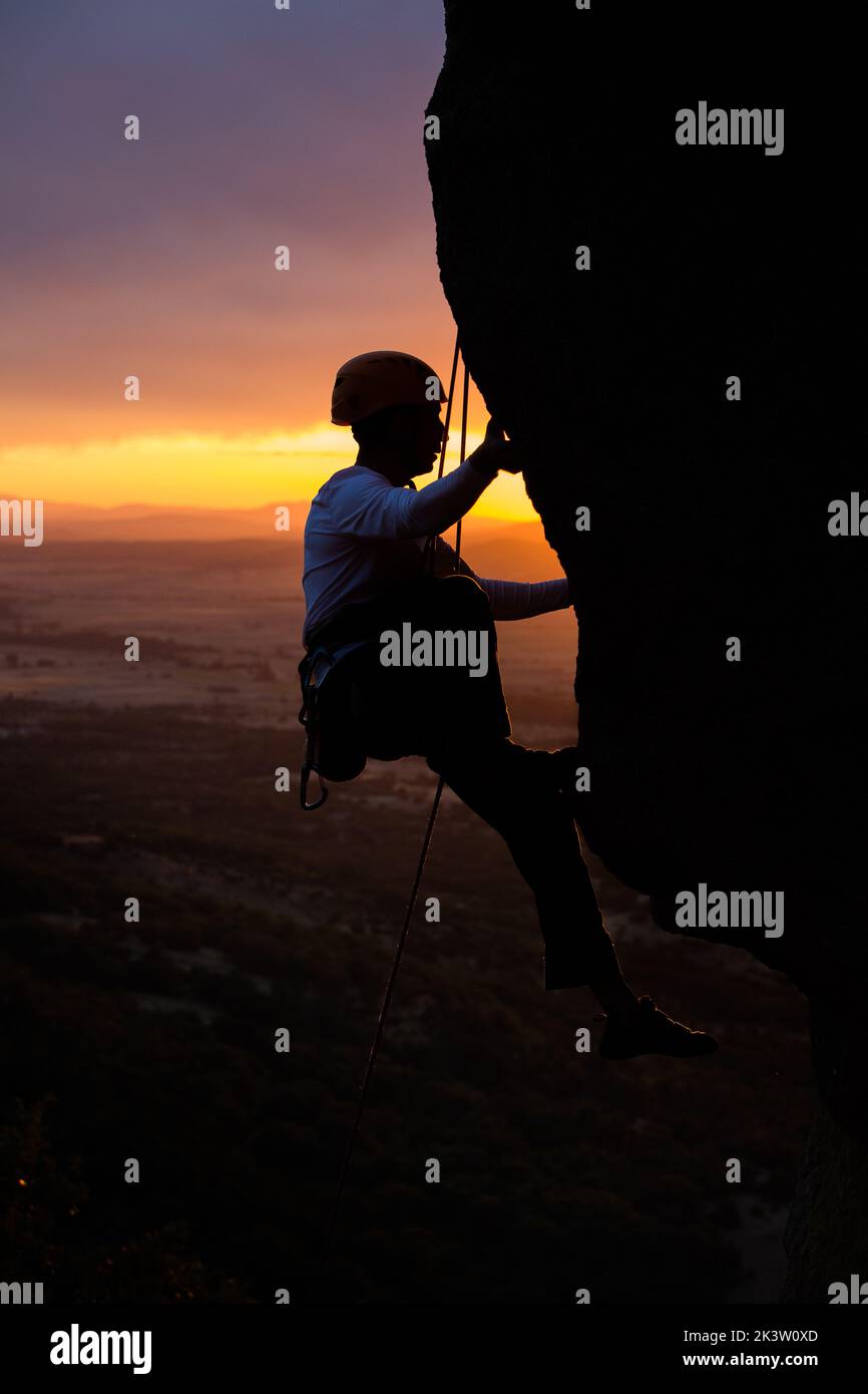Side view of active climber in protective helmet hanging on mountain ...