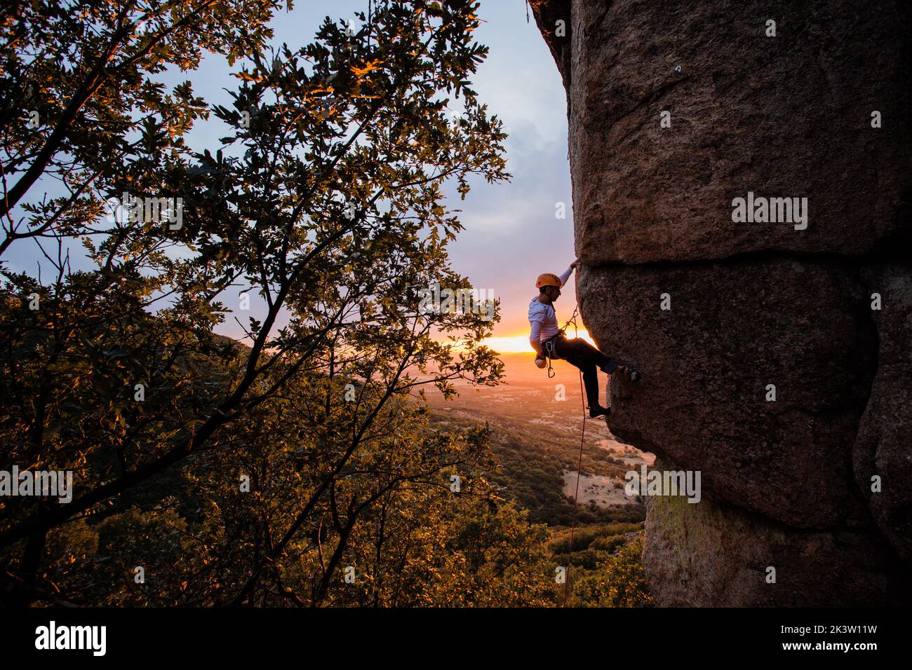 Side view of active climber in protective helmet hanging on mountain ...