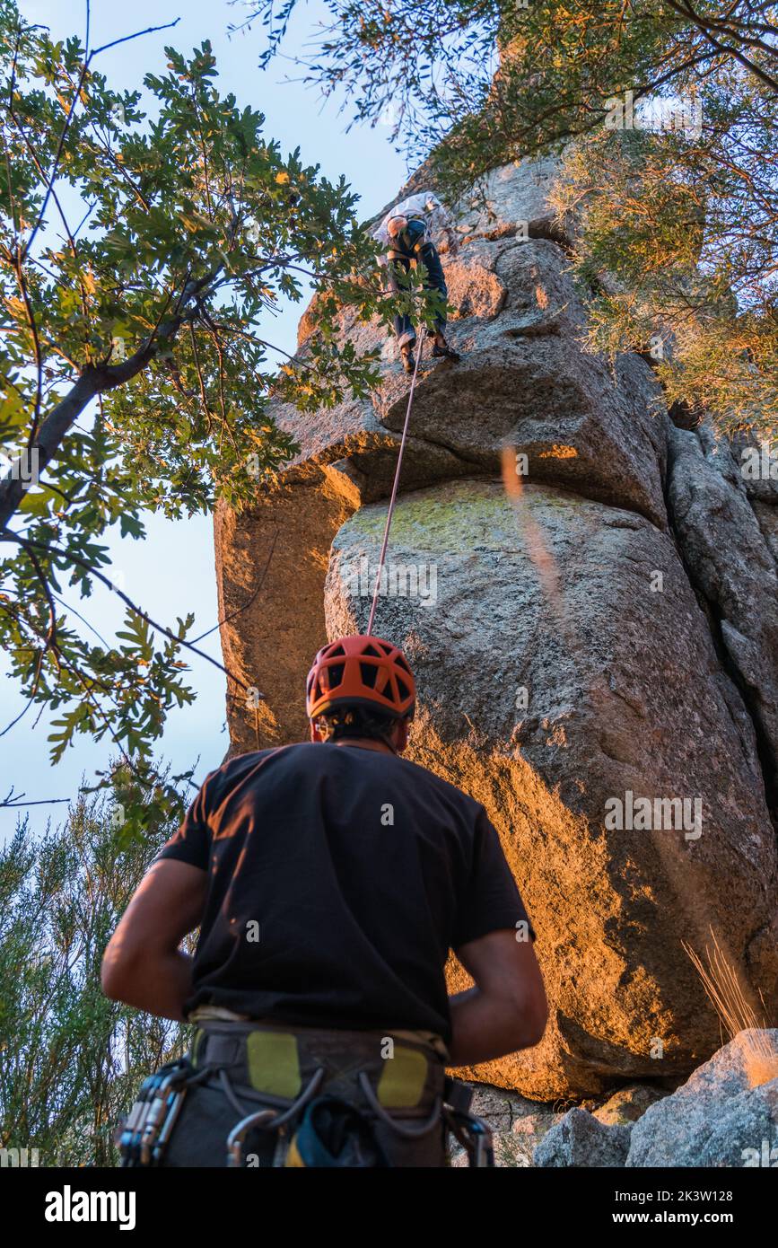 From below climber in helmet holding rope and insuring partner crawling ...