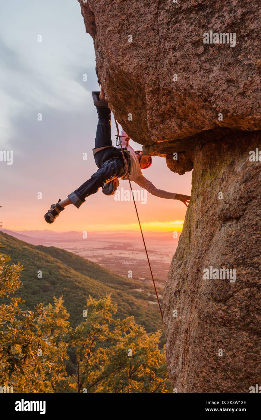 Side view of active climber in protective helmet hanging on mountain ...