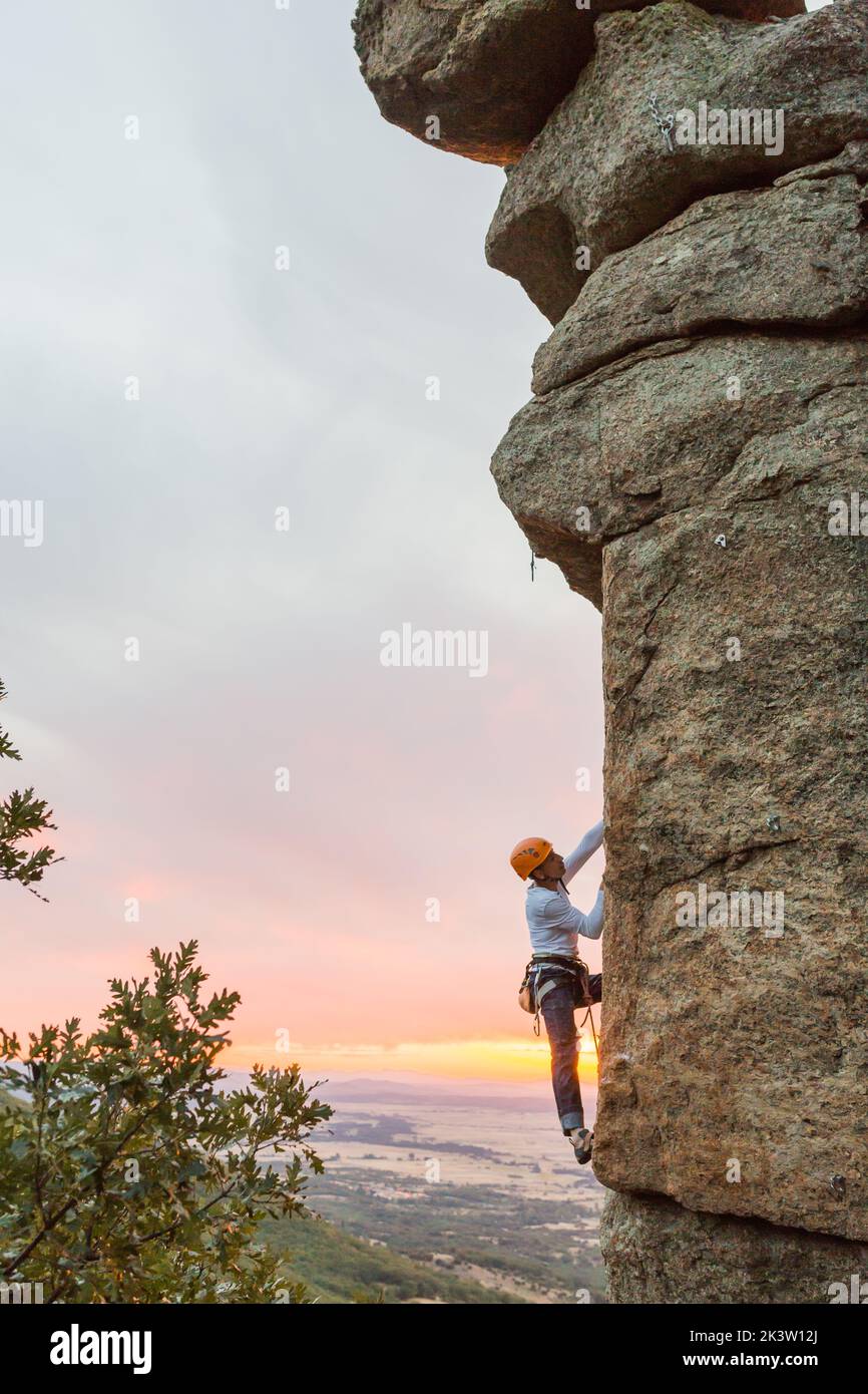 Side view of active climber in protective helmet hanging on mountain ...