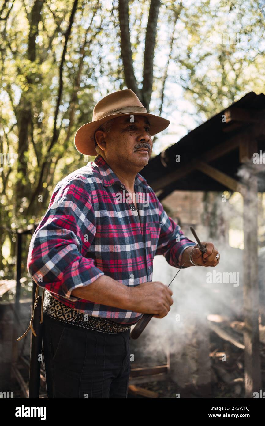 Argentinian male in hat sharpening knife between smoke diffusing in air ...