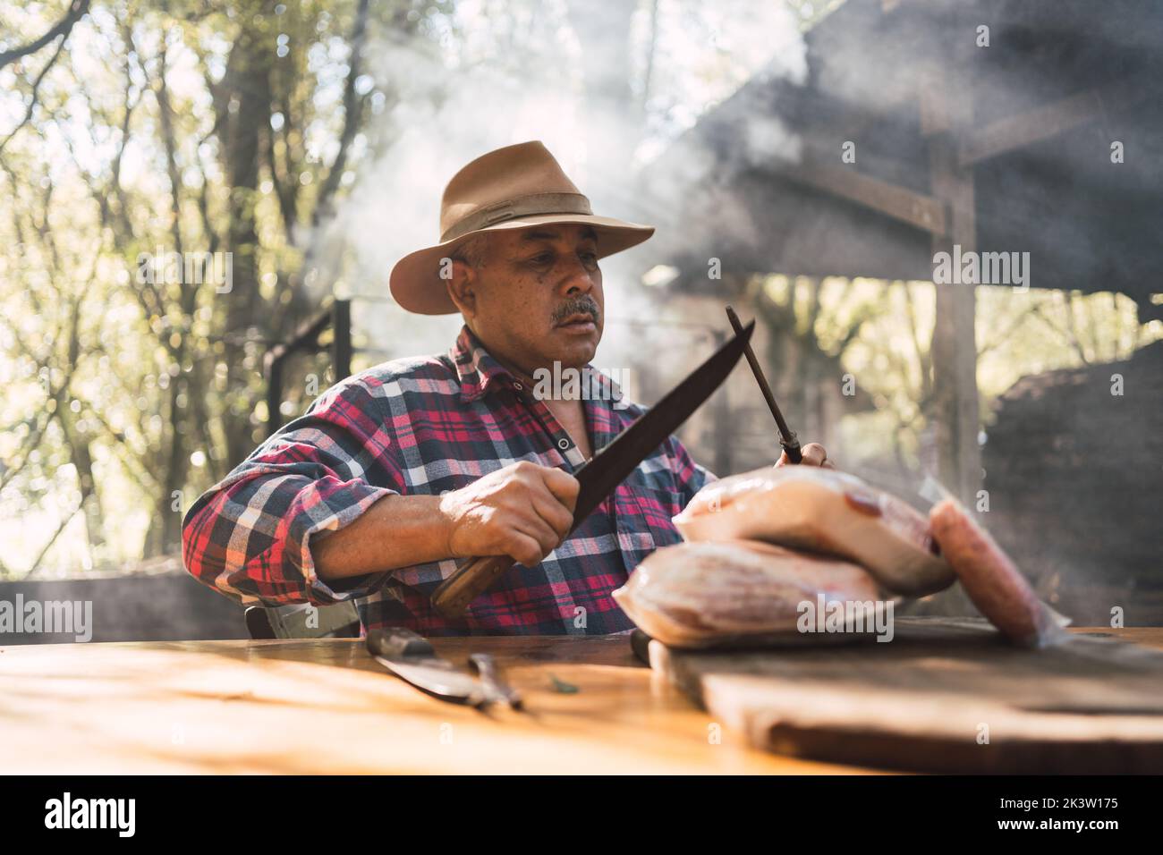 Argentinian male in hat sharpening knife between raw meat with sausages ...