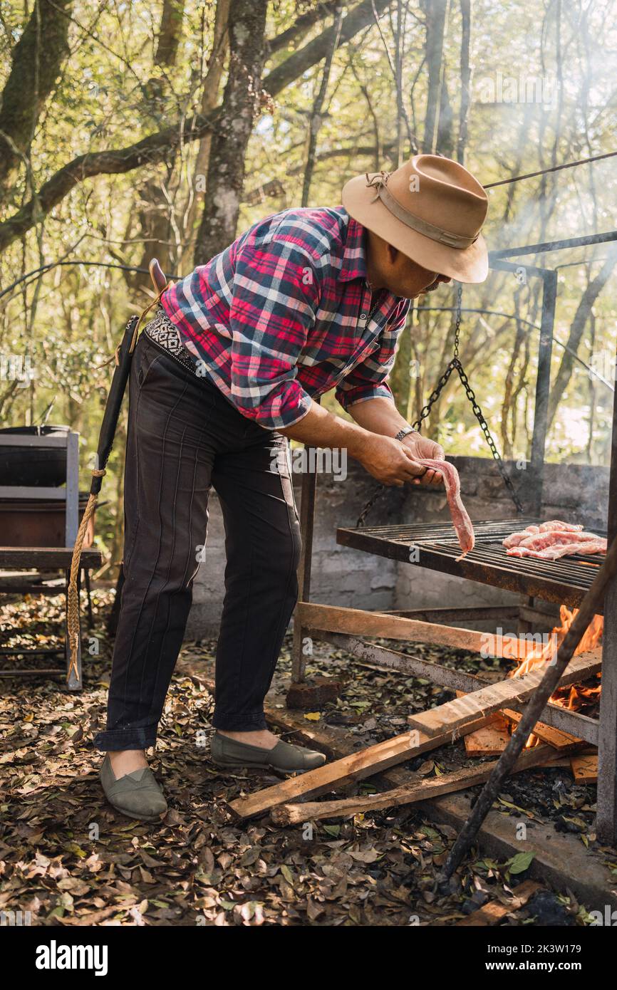 Side view of Argentinian male in hat adjusting fresh meat pieces on ...