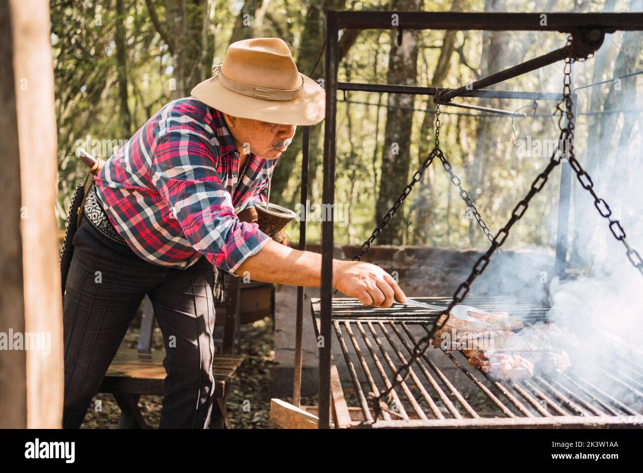 Side view of Argentinian male in hat with fork adjusting fresh meat ...