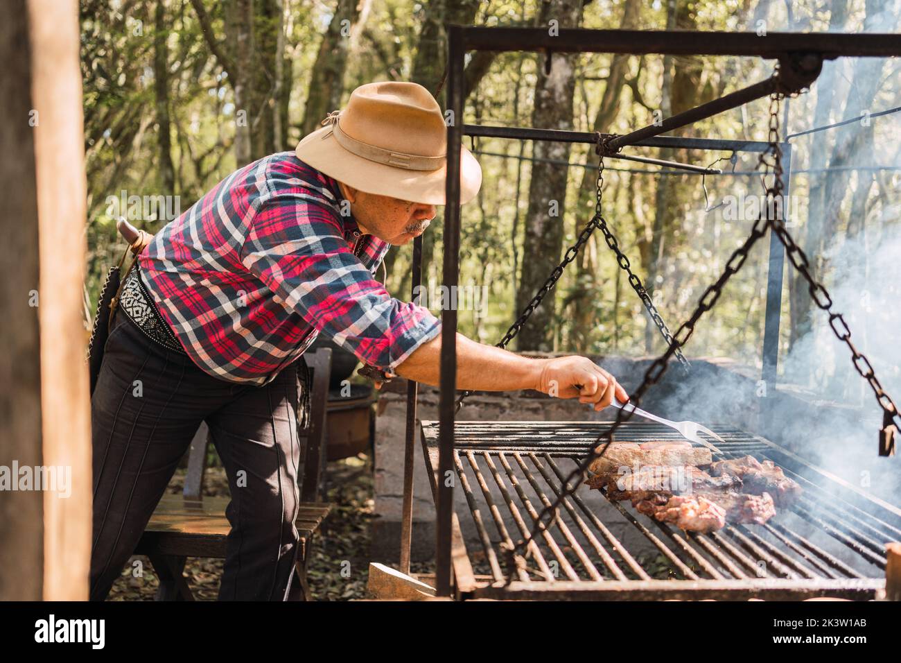 Side view of Argentinian male in hat with fork adjusting fresh meat ...