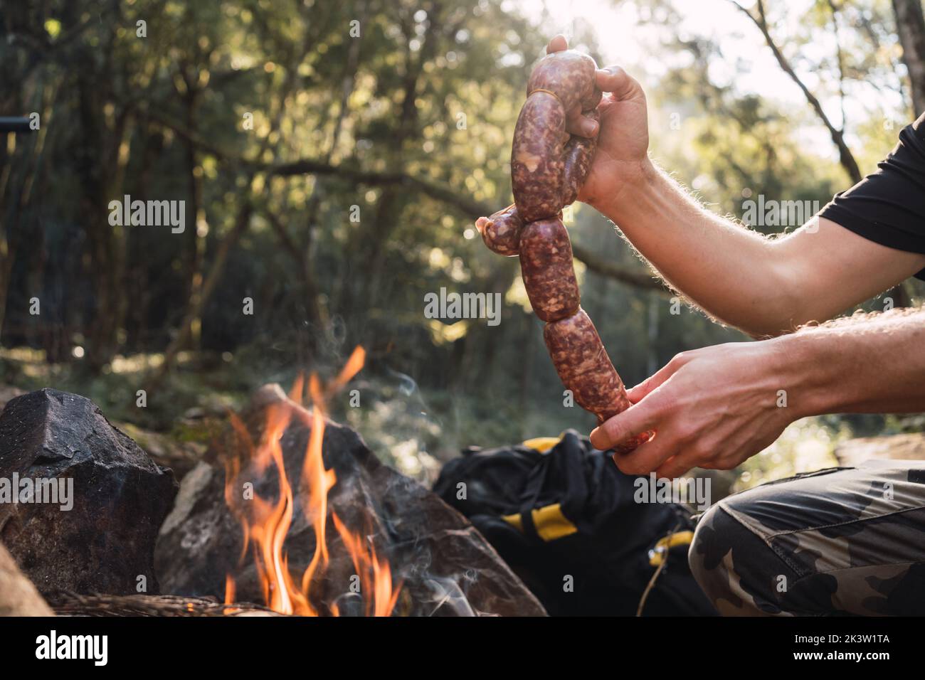 Crop unrecognizable male tourist putting raw beef sausages on barbecue ...