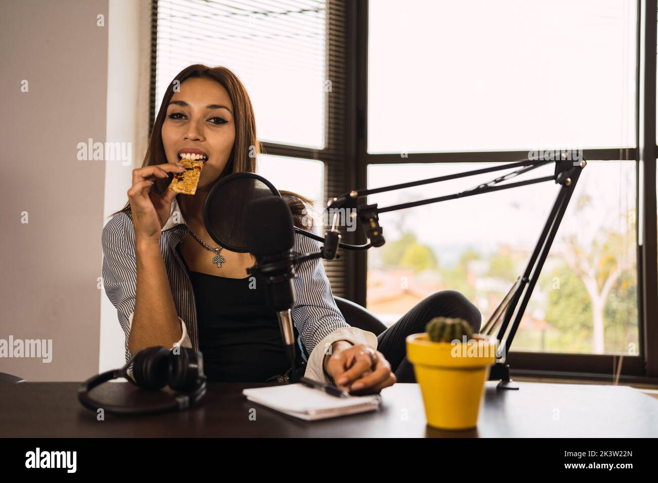 Female radio host eating snack at table with microphone headphones and ...