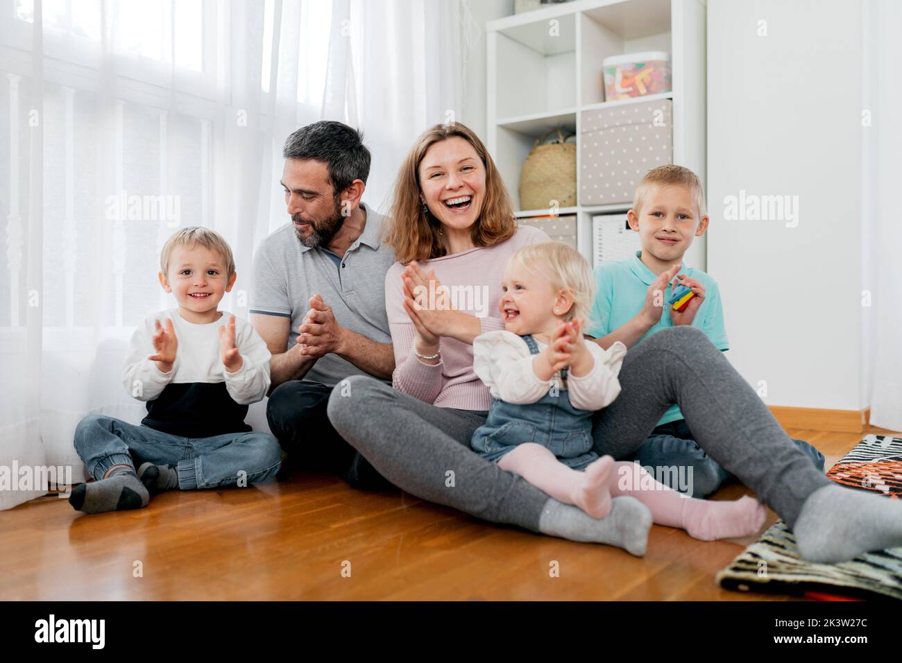 Content adult parents with charming children having fun on parquet ...