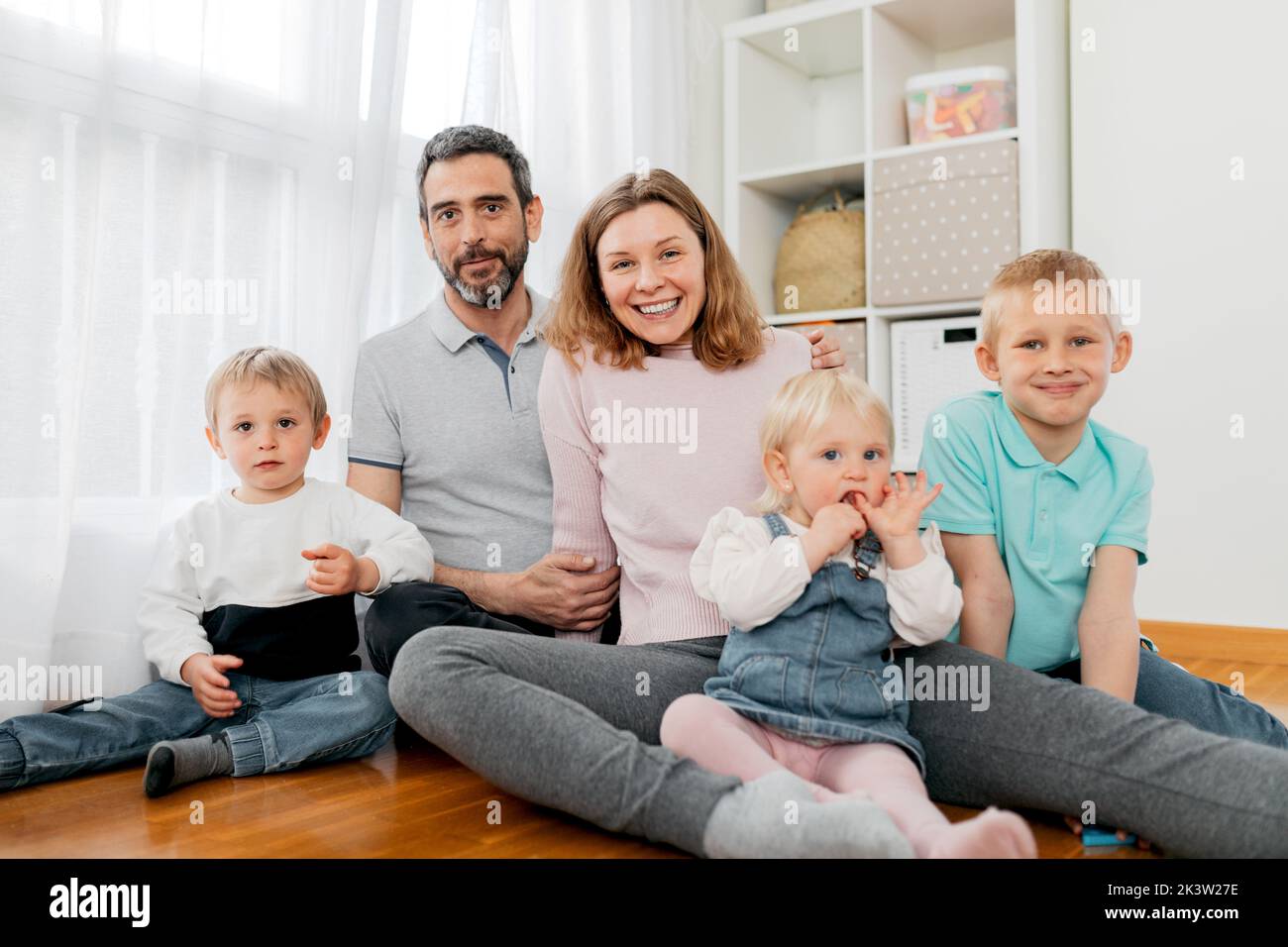 Content adult parents with charming children having fun on parquet ...