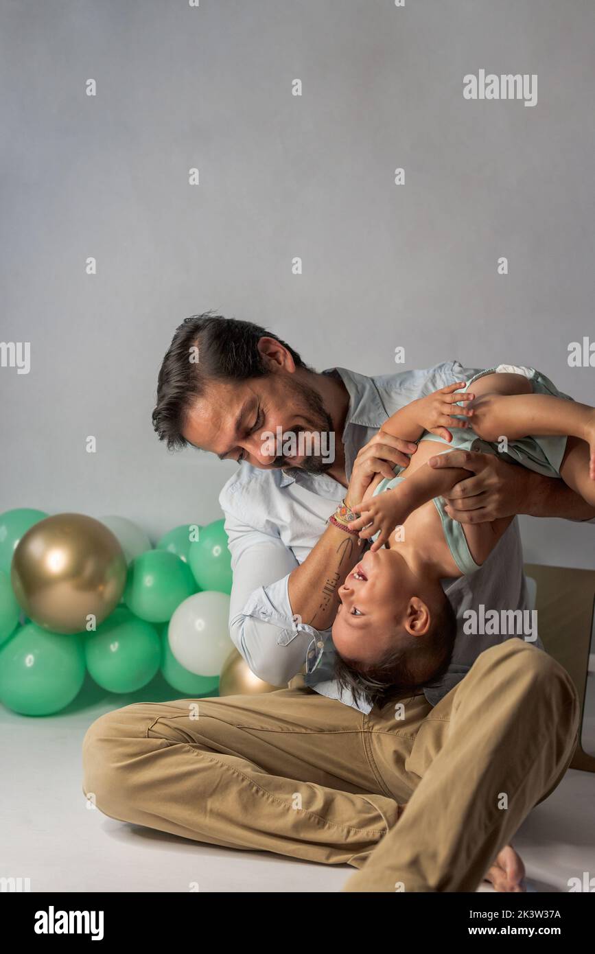 Father playing with small baby while holding legs and tickling in ...