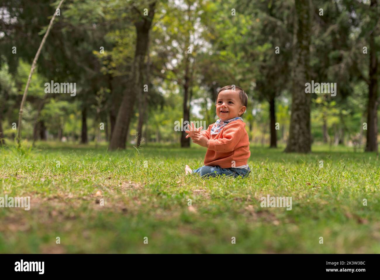 Adorable barefoot ethnic baby boy clapping hands on grassy lawn against ...