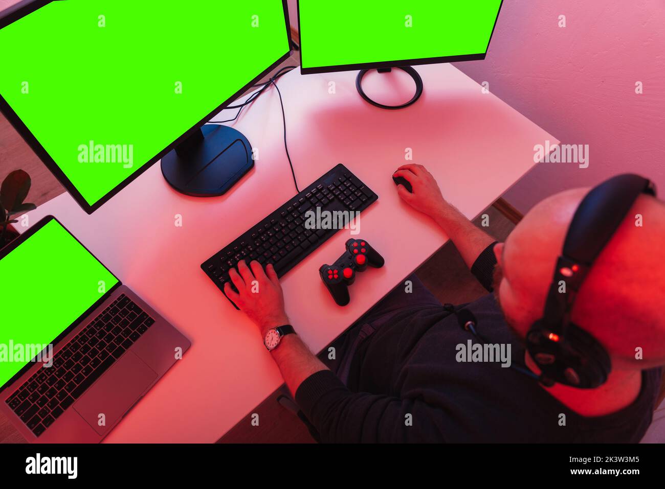 Bald man is sitting and playing in front of three green screen ...