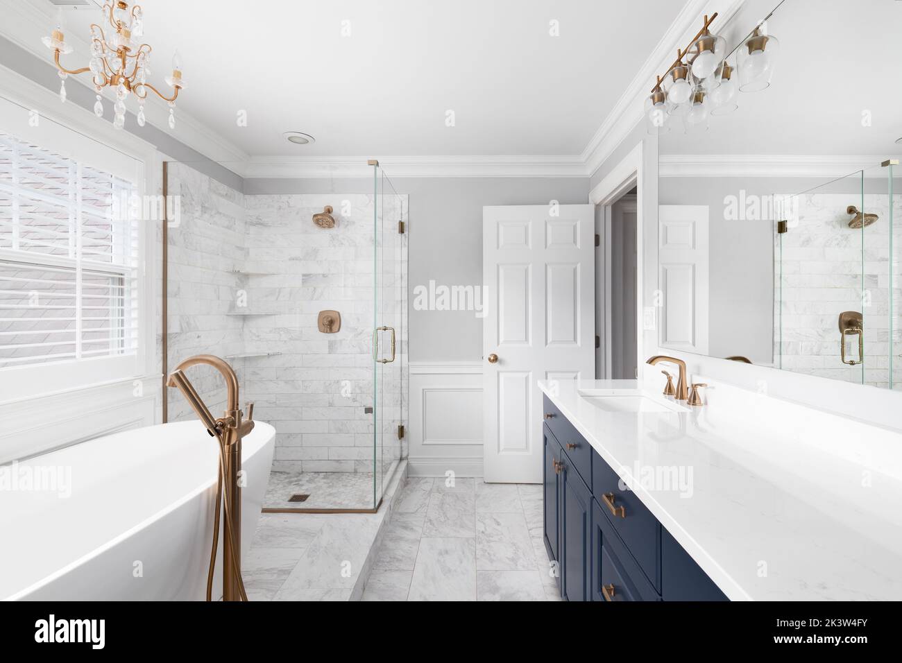 A beautiful bathroom with a blue vanity cabinet, standalone bathtub and shower, and gold faucets ...