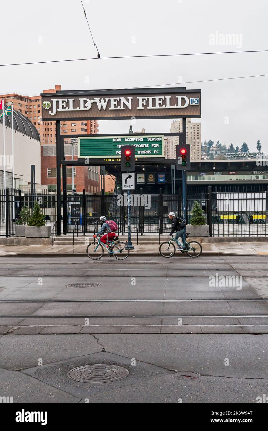 Two cyclists ride bicycles past Jeld Wen Field gate as viewed across SW ...