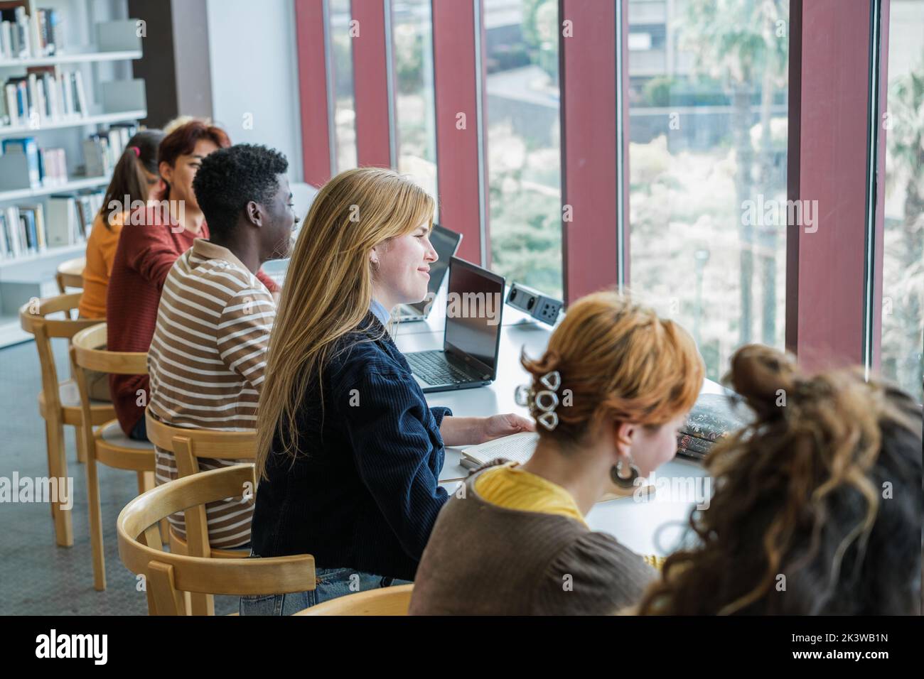 College students studying together in a brightly lit library with a ...