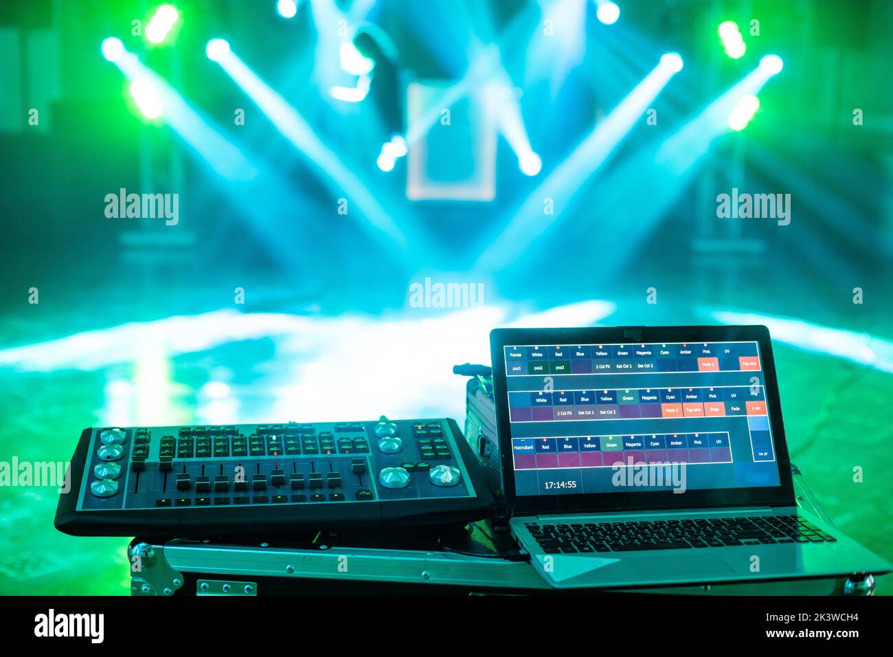 Highlighted deejay mixing with laptop on the stage with blue beams and ...