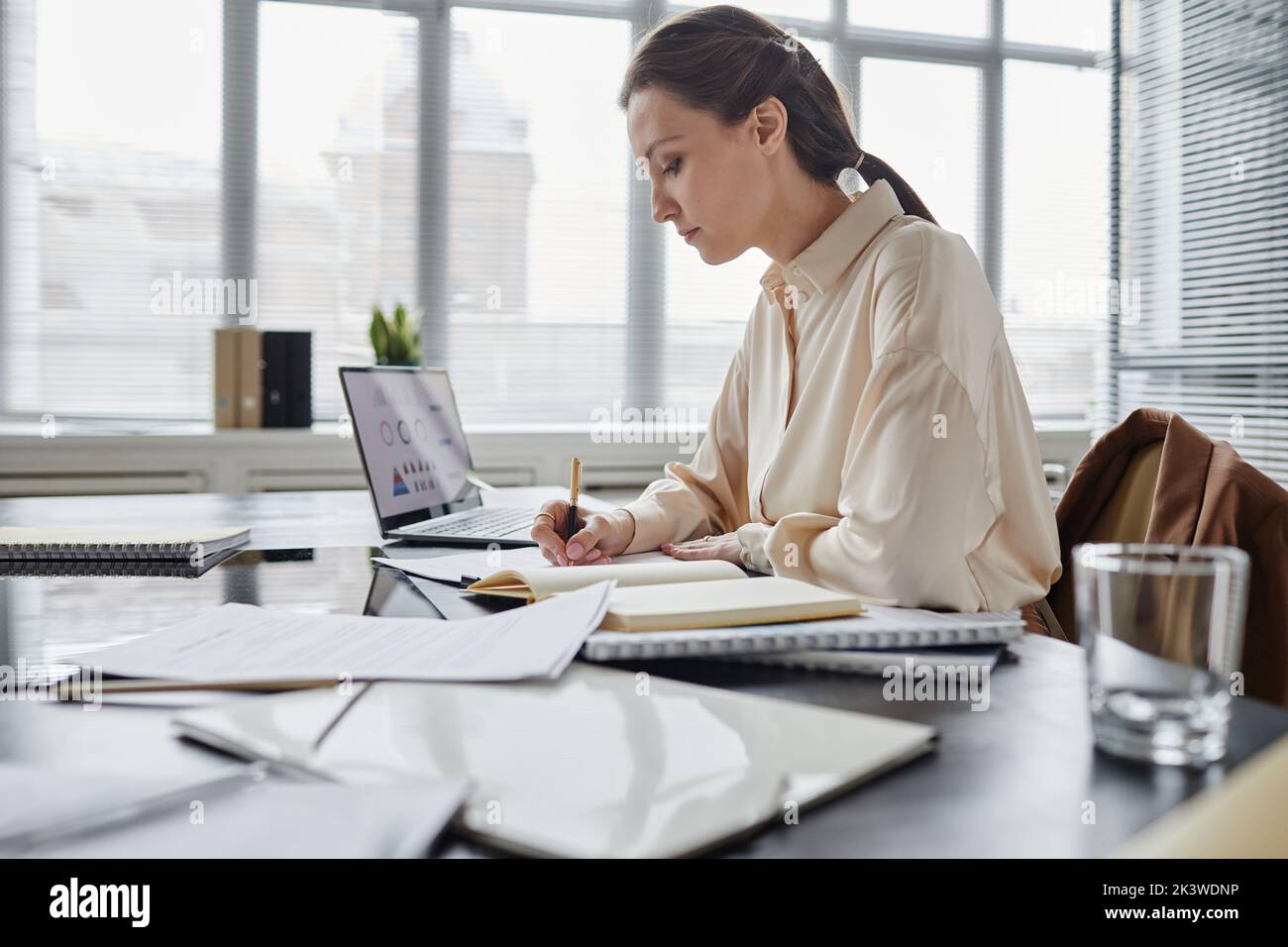 Side view portrait of young female boss taking notes while working at ...