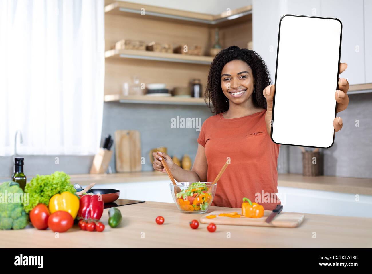 Cheerful millennial black lady cuts organic vegetables at salad, shows ...