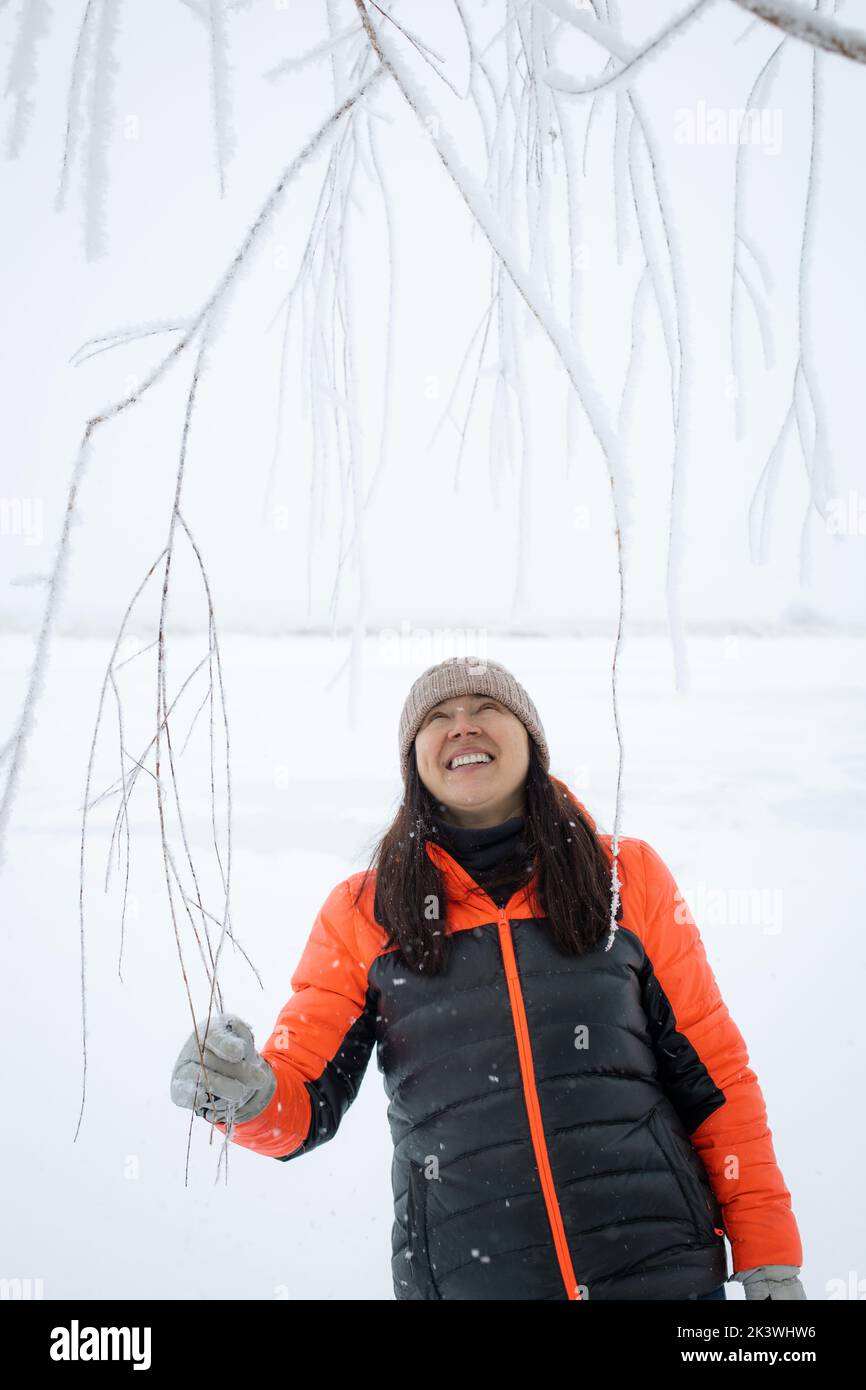 Blissful woman pulling twigs covered with snow with hand in glove ...