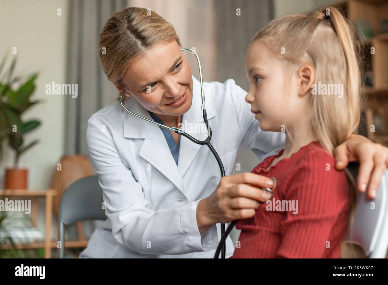 Caring female cardiologist holding stethoscope and listening to girl ...