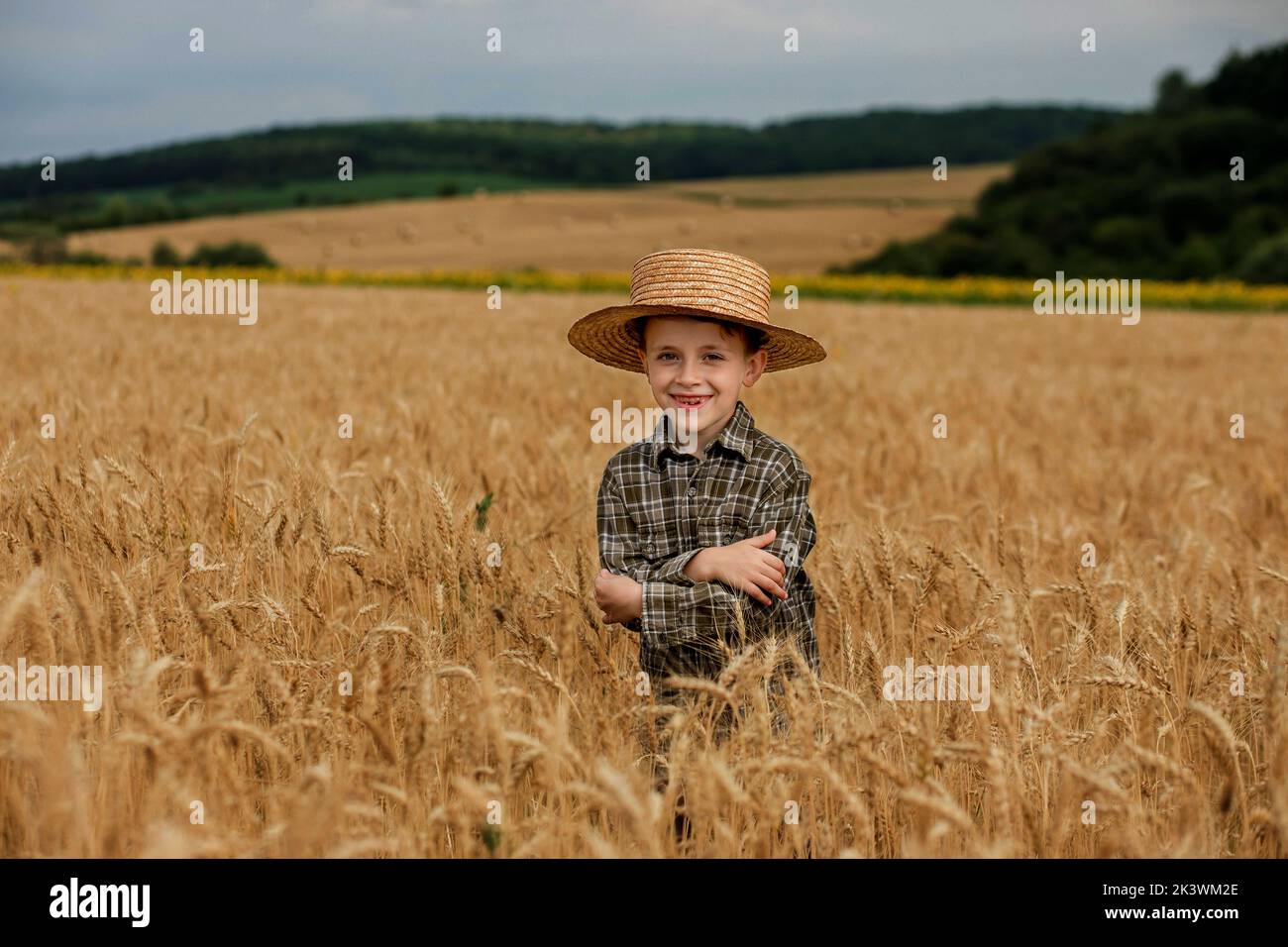 A smiling little farmer boy in a plaid shirt and straw hat poses for a ...