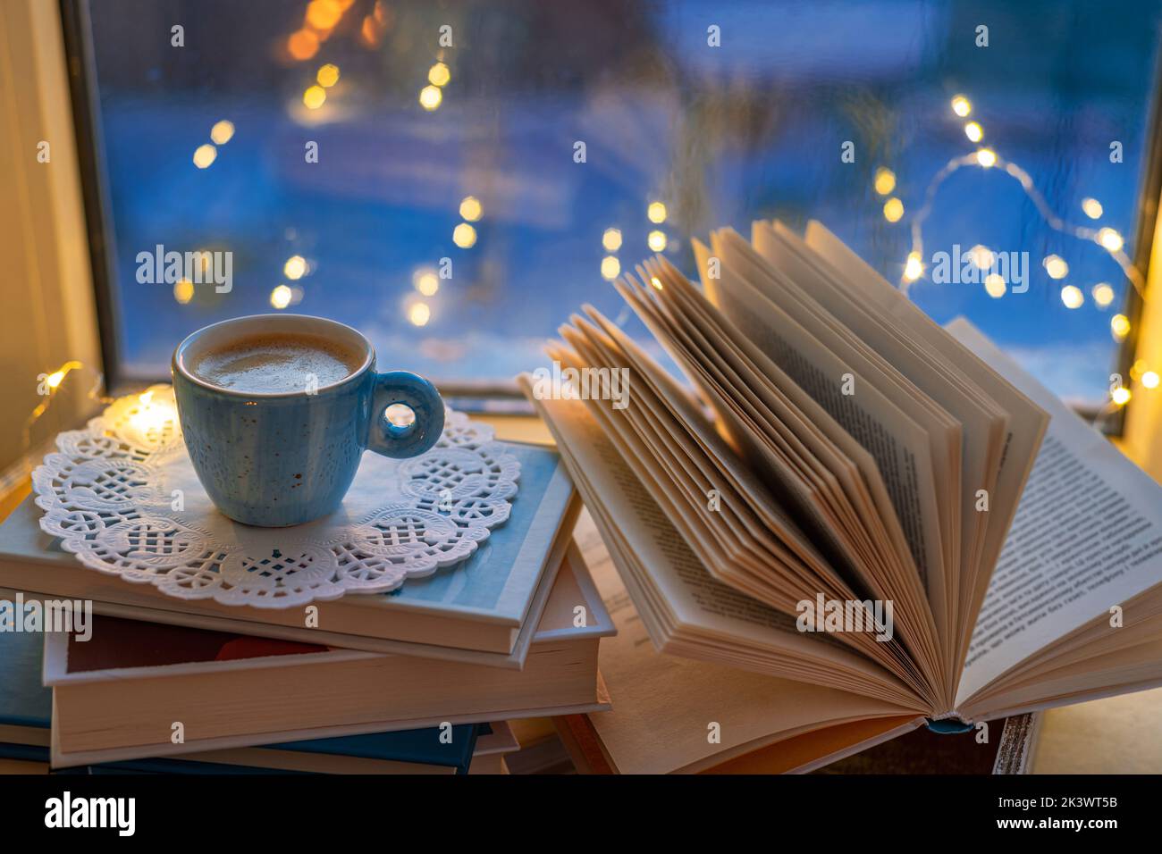 Coffee cup, open book, fairy lights on window sill on blue blurred ...