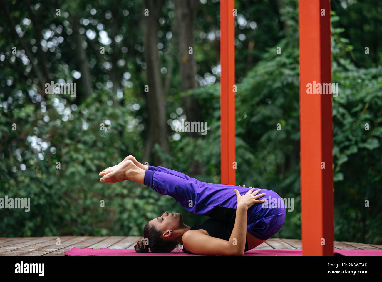 Lying on a back, young beautiful woman bends her legs to the chest ...