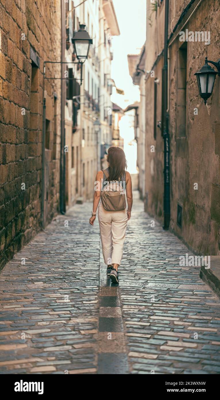 woman looking to the side as she walks down a street in Hondarribia ...