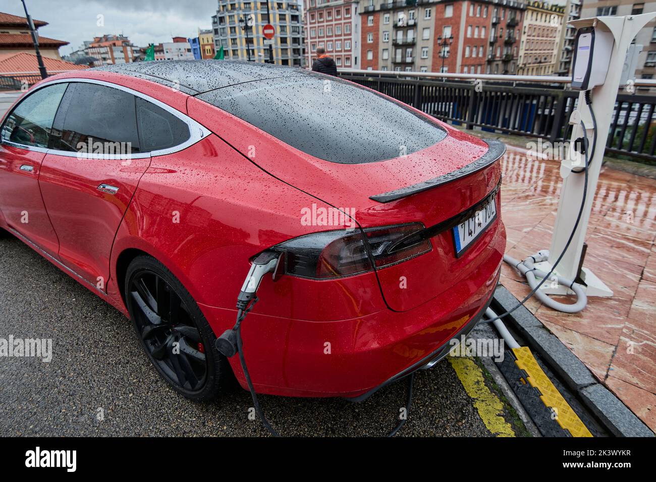 Red electric car charging in the street on a rainy day. Concept of the ...