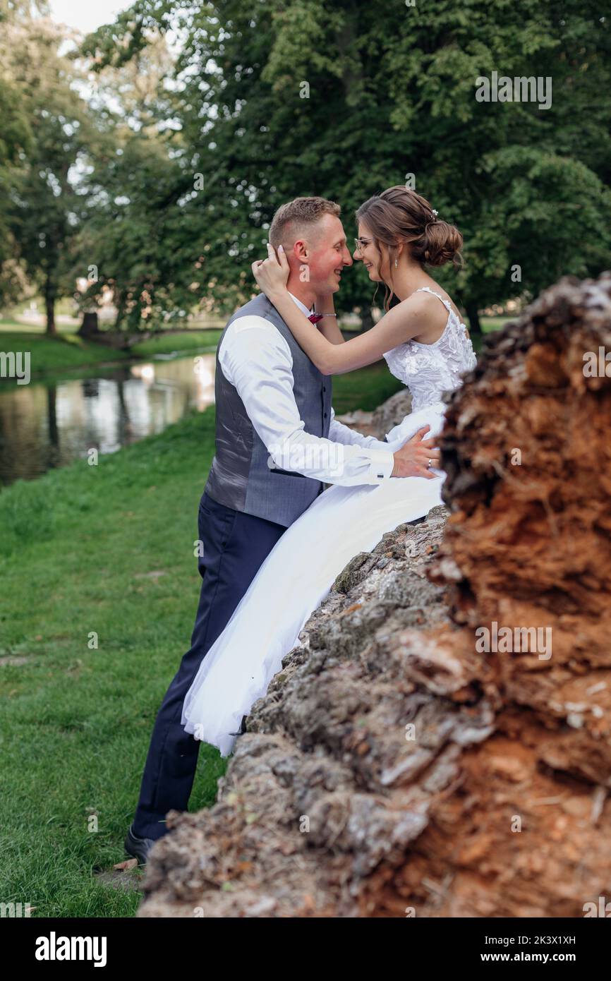 Side view of wedding couple standing near trees. Young woman sitting on ...