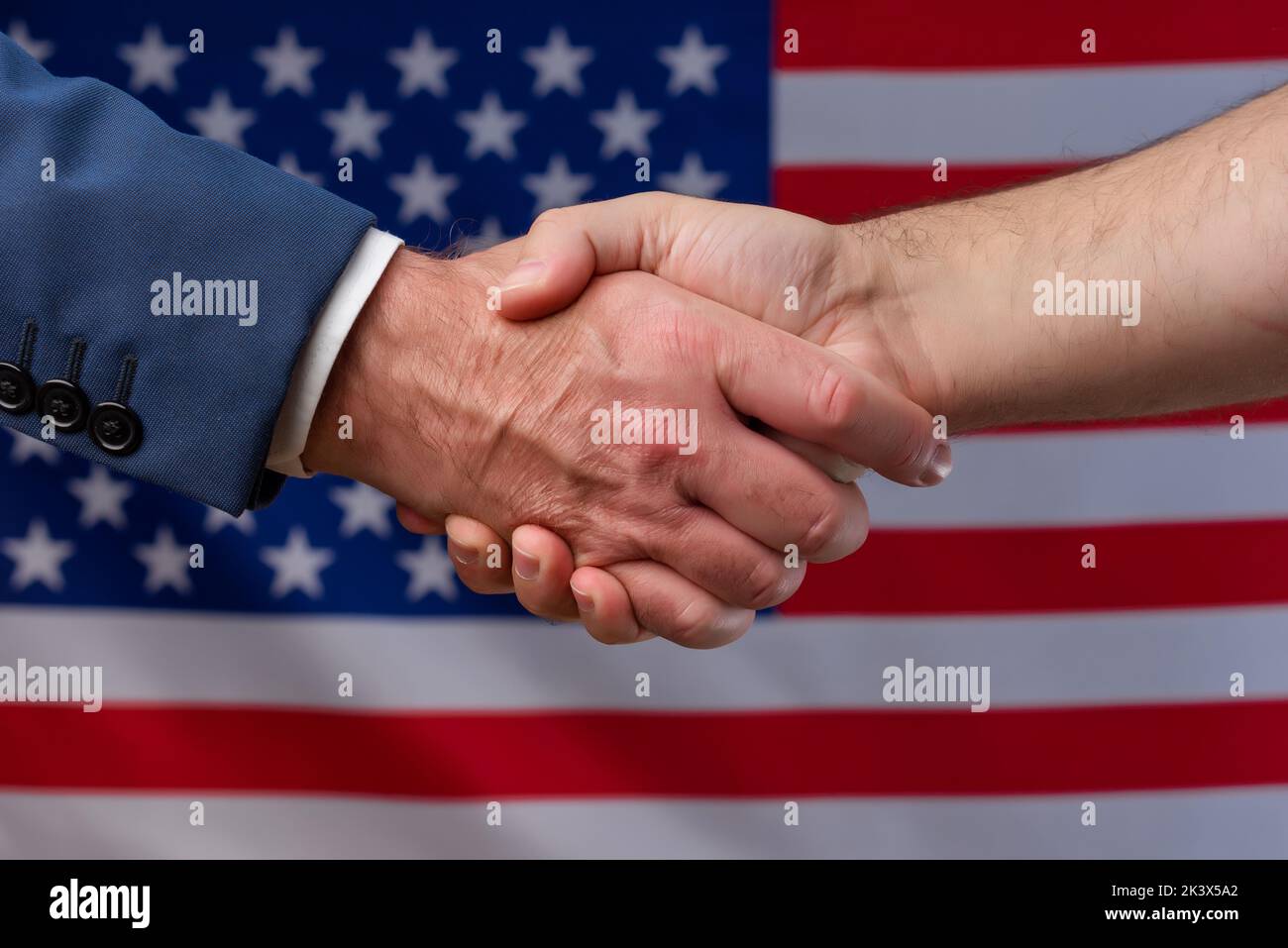 Two men shaking hands with the United States flag in the background ...