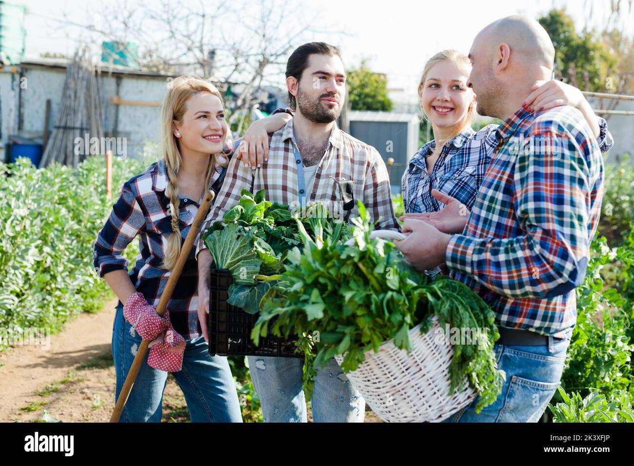 Happy family of four gardeners holding harvest of vegetables and greens ...