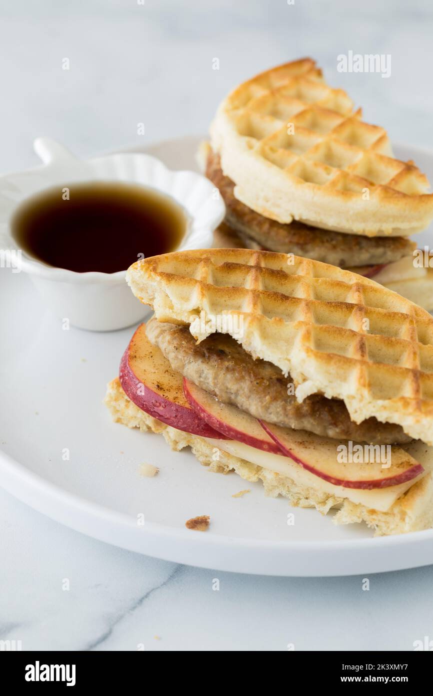 A homemade waffle and sausage sandwich served with maple syrup for ...