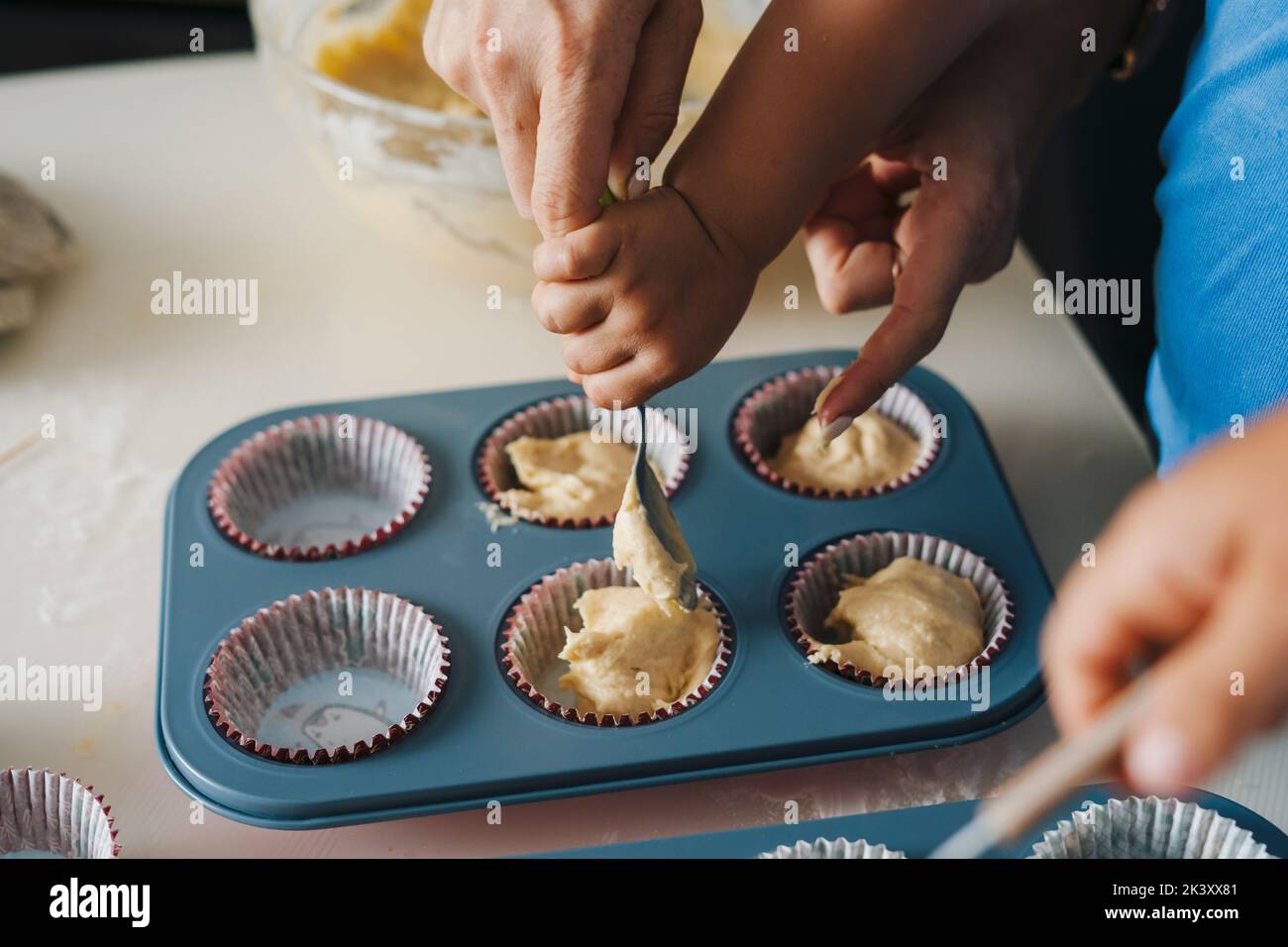 Family cooking in the kitchen pouring raw dough into silicone forms to ...