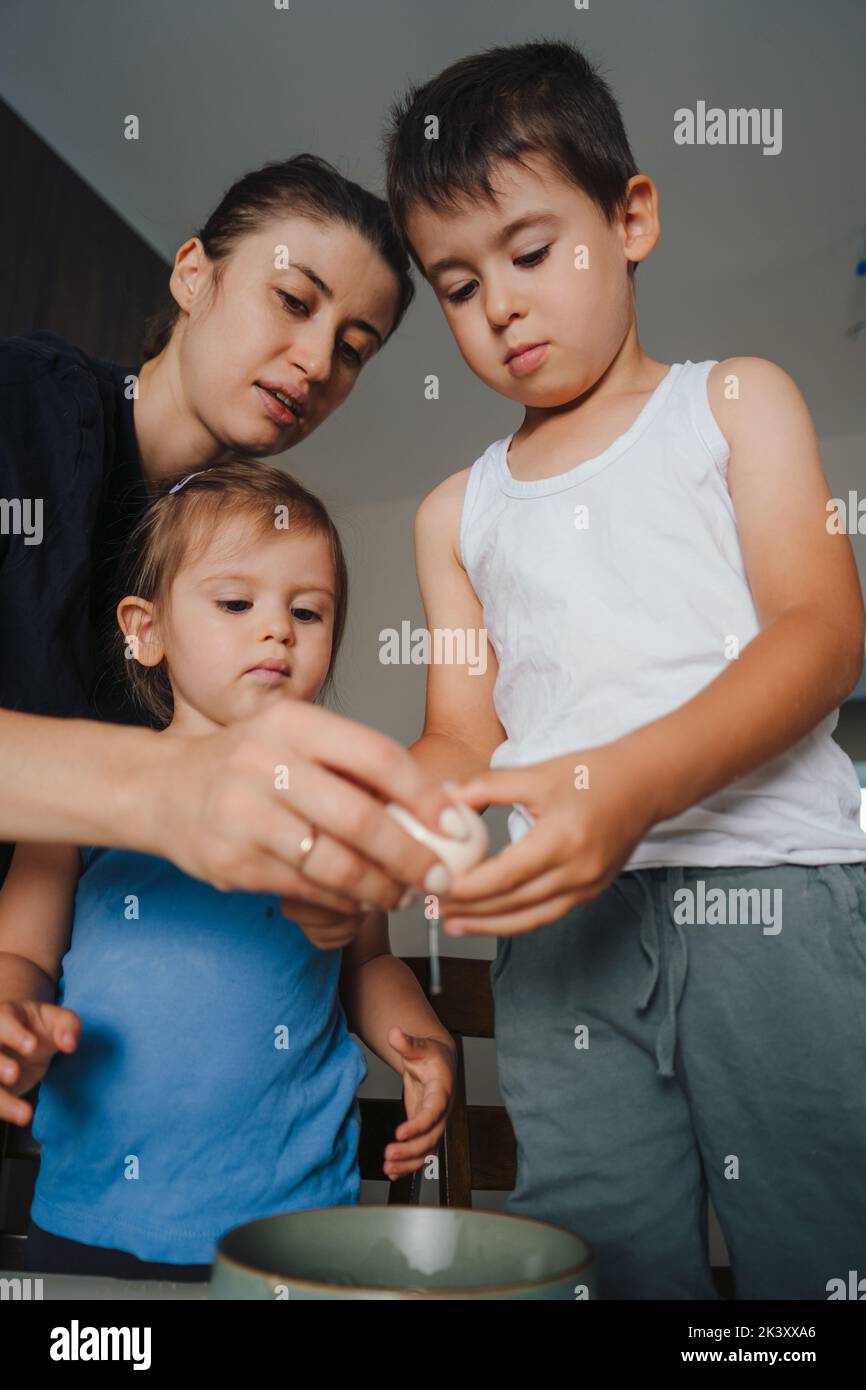 Caucasian mother teaching showing her son child how to break eggs into ...