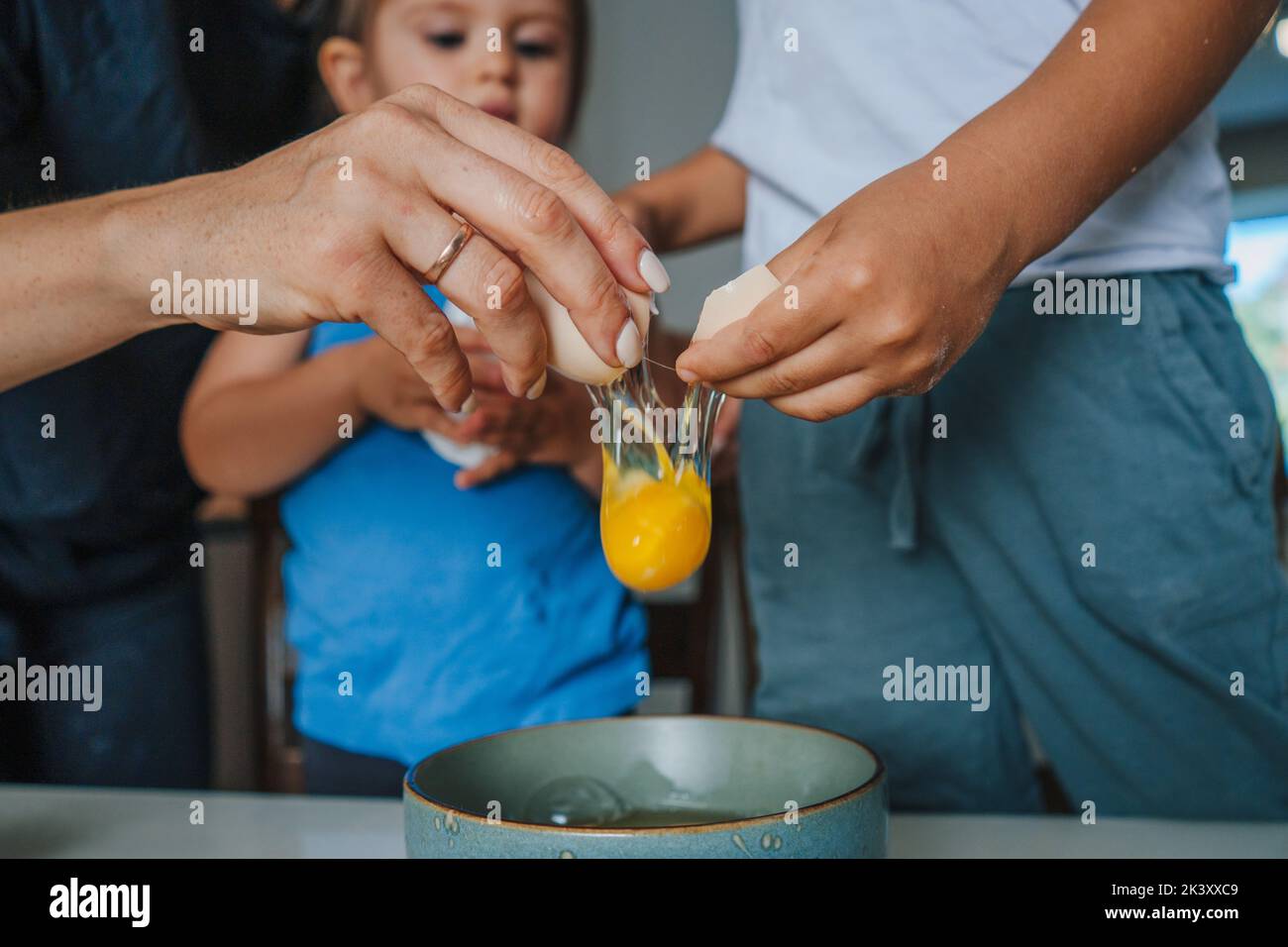 Mother hands breaking eggs in bowl with her two children while making ...