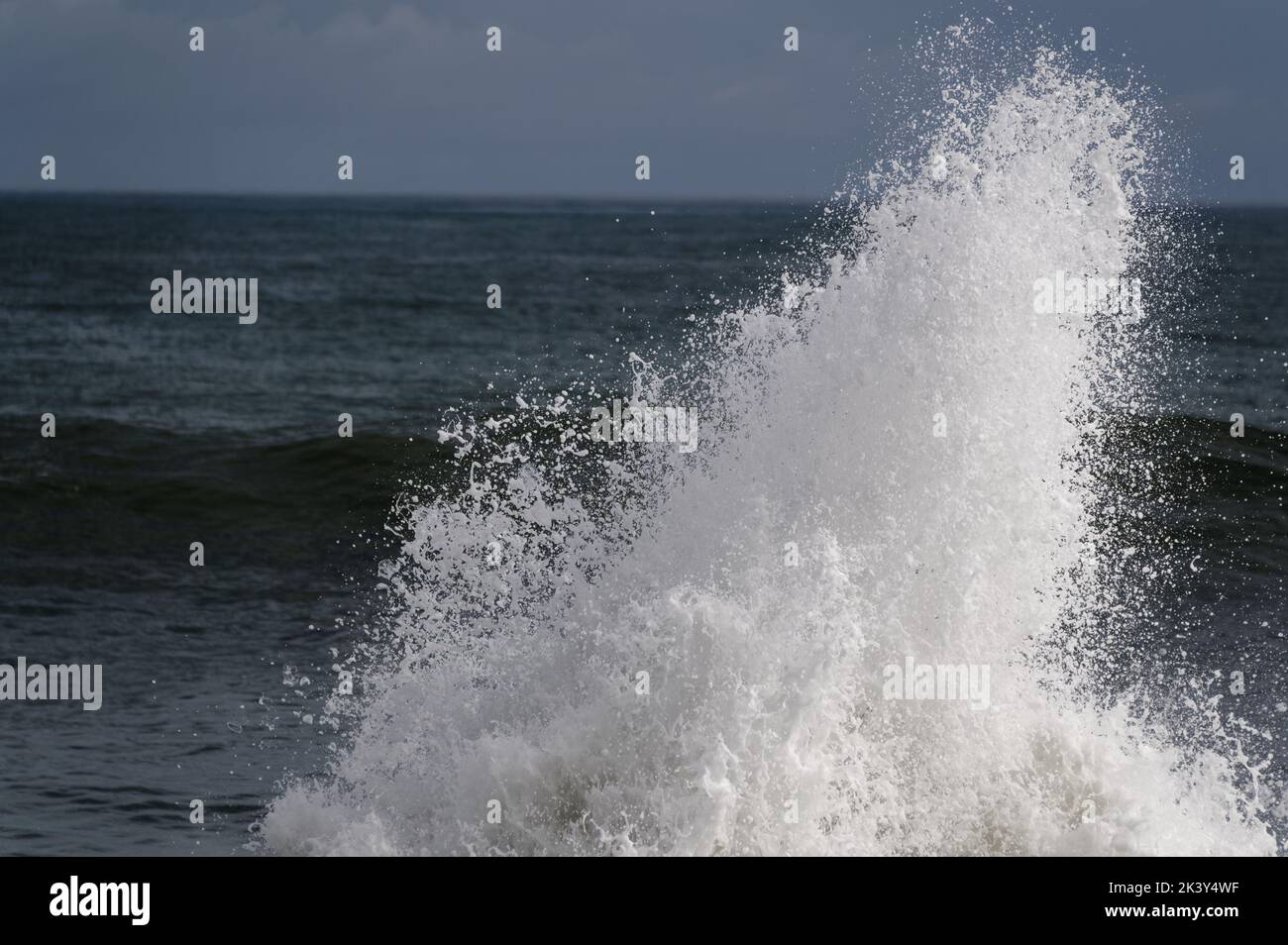 Froth from a wave is pointing high into the sky. The camera has caught ...