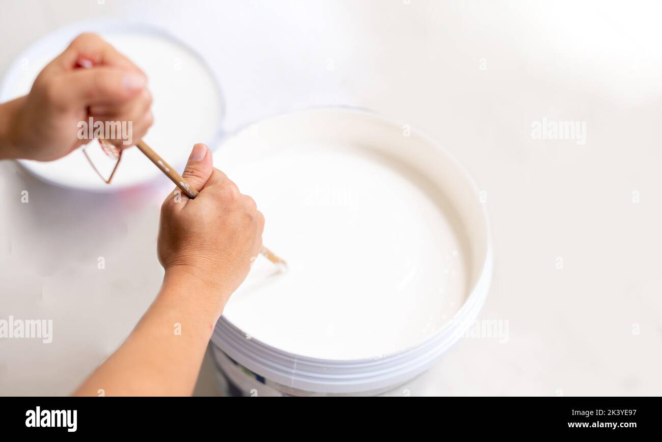 Female hand use the woodstick to mix paint into the tray and dips ...