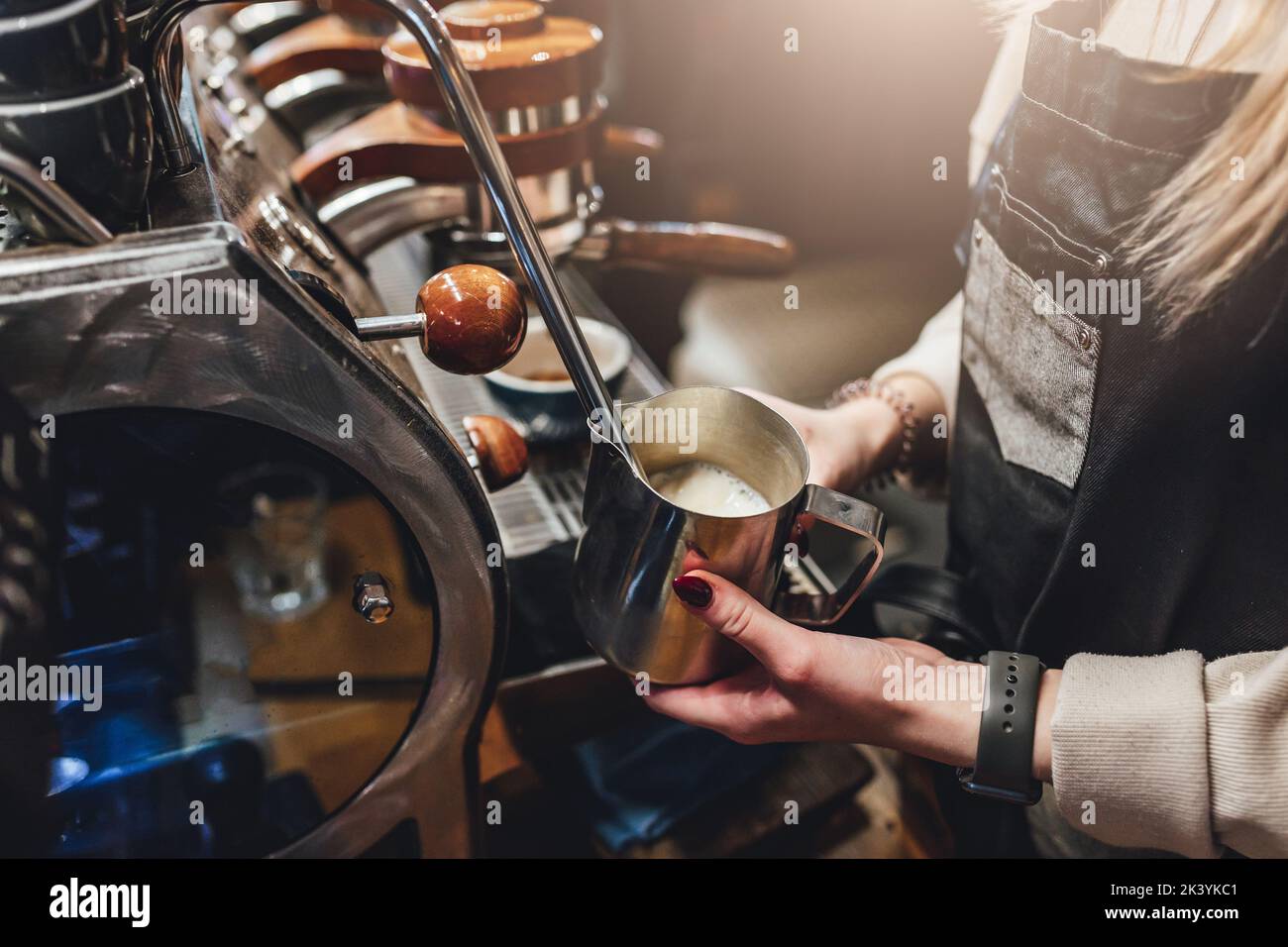 A closeup of a female barista steaming milk for coffee in coffee shop ...