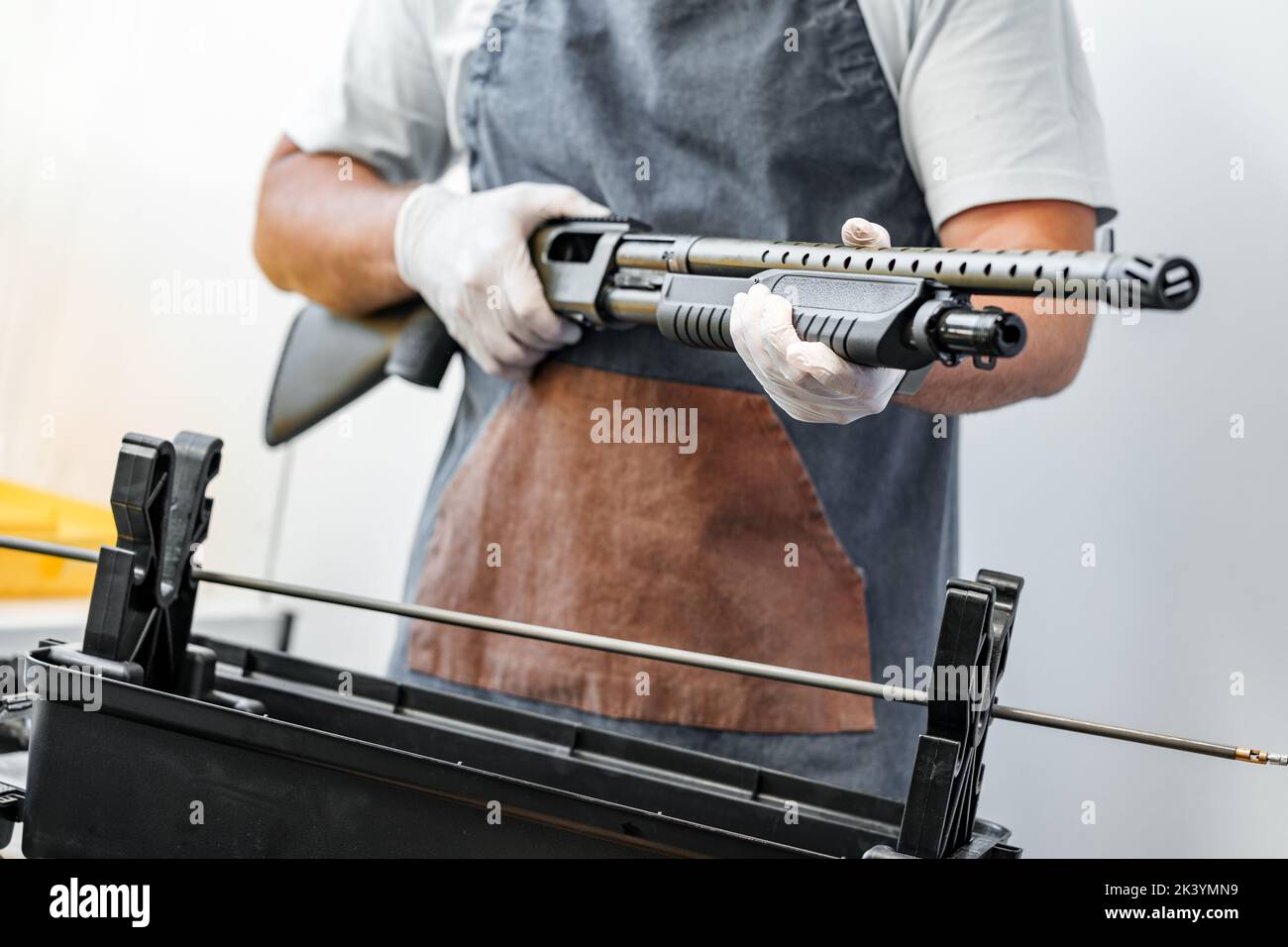 Close up of young man in apron disassembling a gun above the table ...