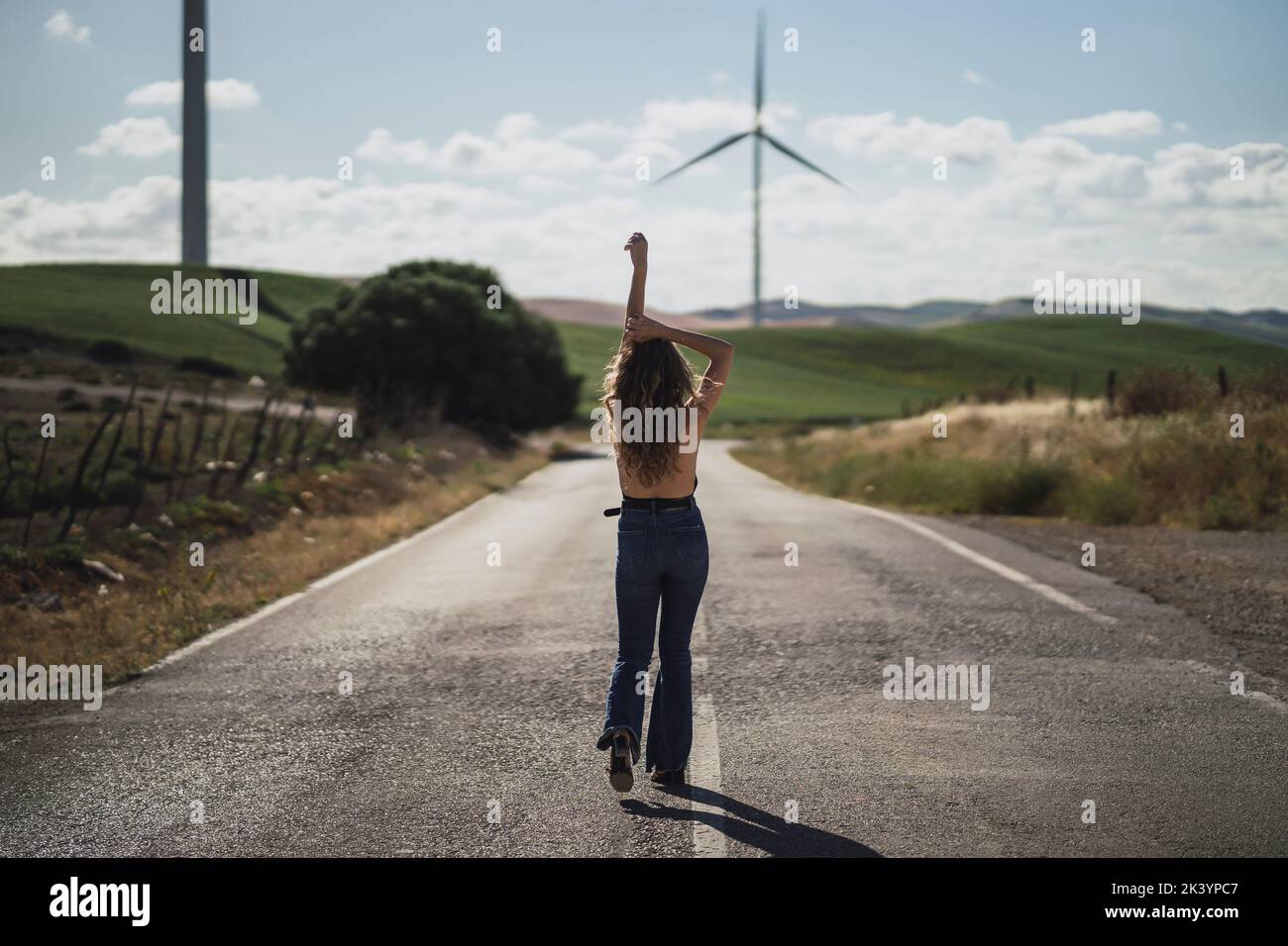 A back view of a young Caucasian female on a road with a blur ...