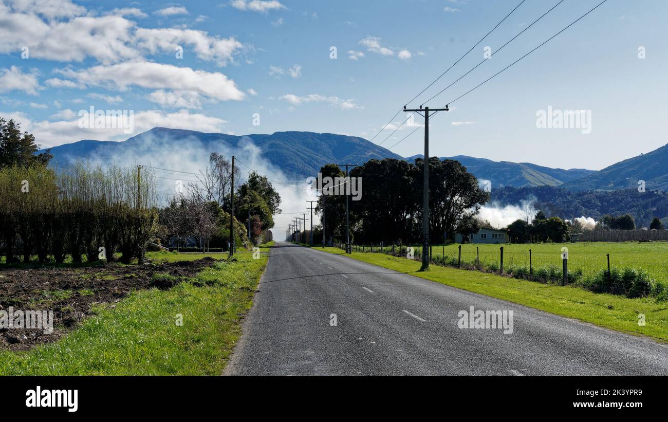 Smoke from an orchard prunings burn off bonfire obscuring a road ...
