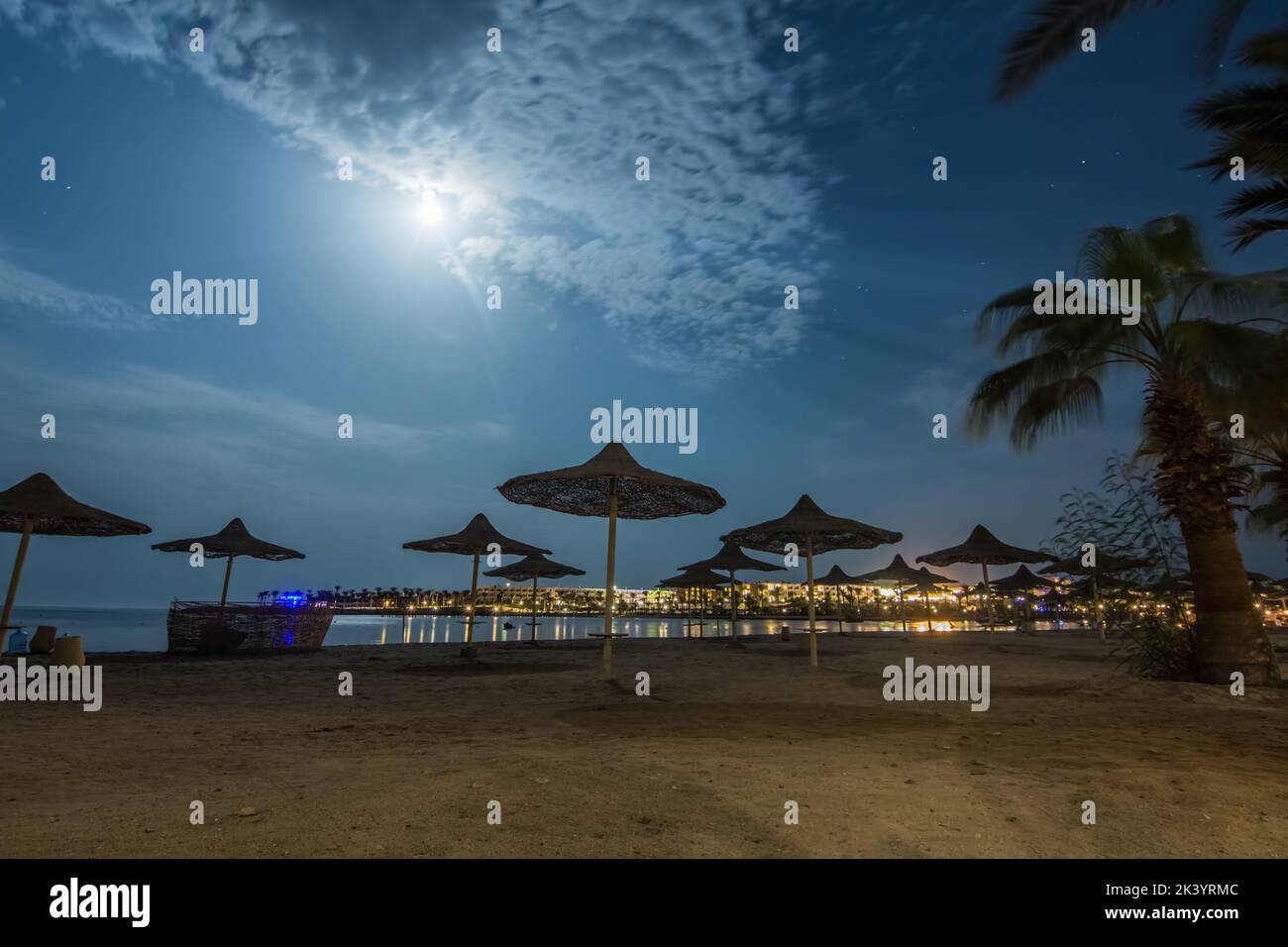 sandy beach with beach umbrellas and a bright moon in the night in ...
