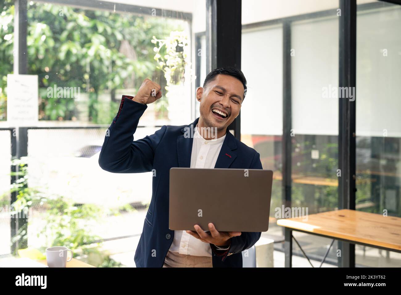 Happy young businessman in suit looking at laptop excited by good news ...