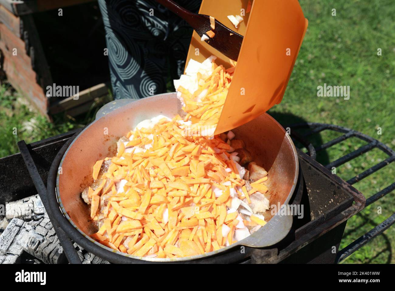 Chef adding carrots and onions to cauldron with meat for pilaf Stock ...
