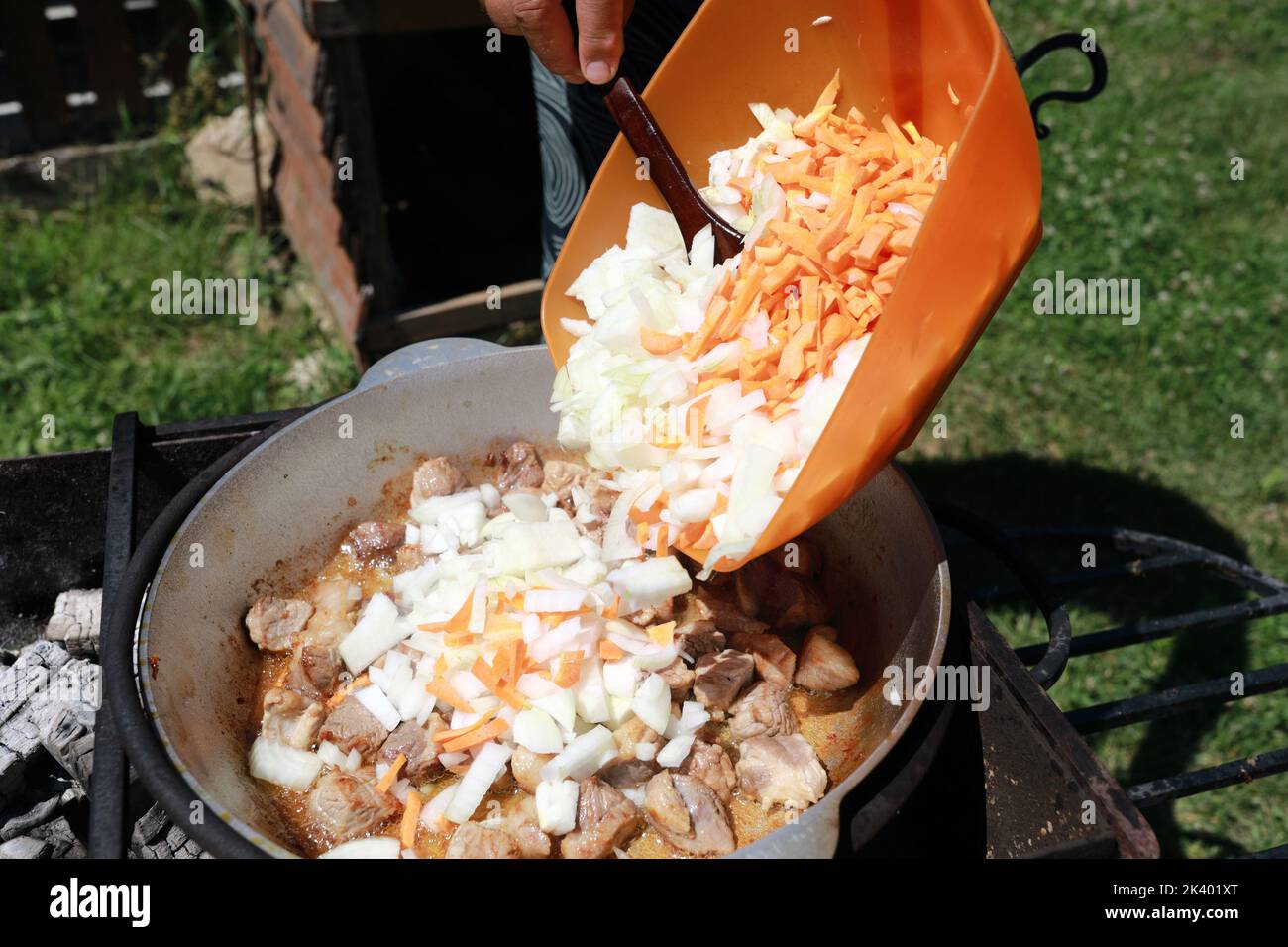 Man adding carrots and onions to cauldron with meat for pilaf Stock ...