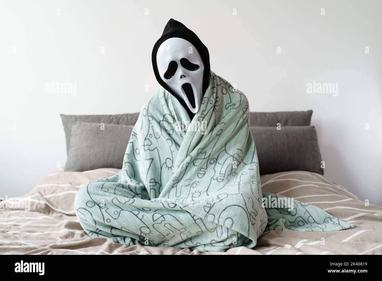 Unrecognised person in ghost sad mask in plaid freezing at home. Cold ...