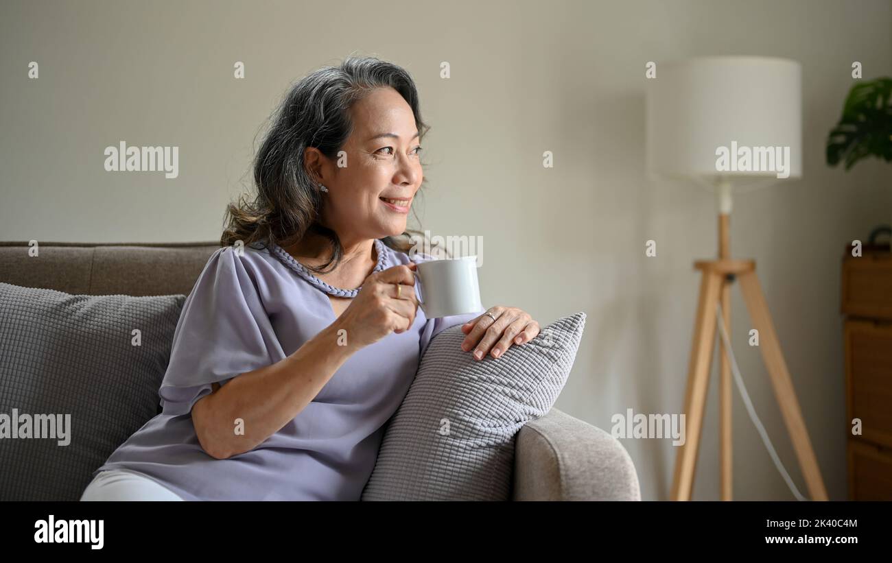 Happy and calm Asian 60s aged-woman sipping her morning coffee while ...